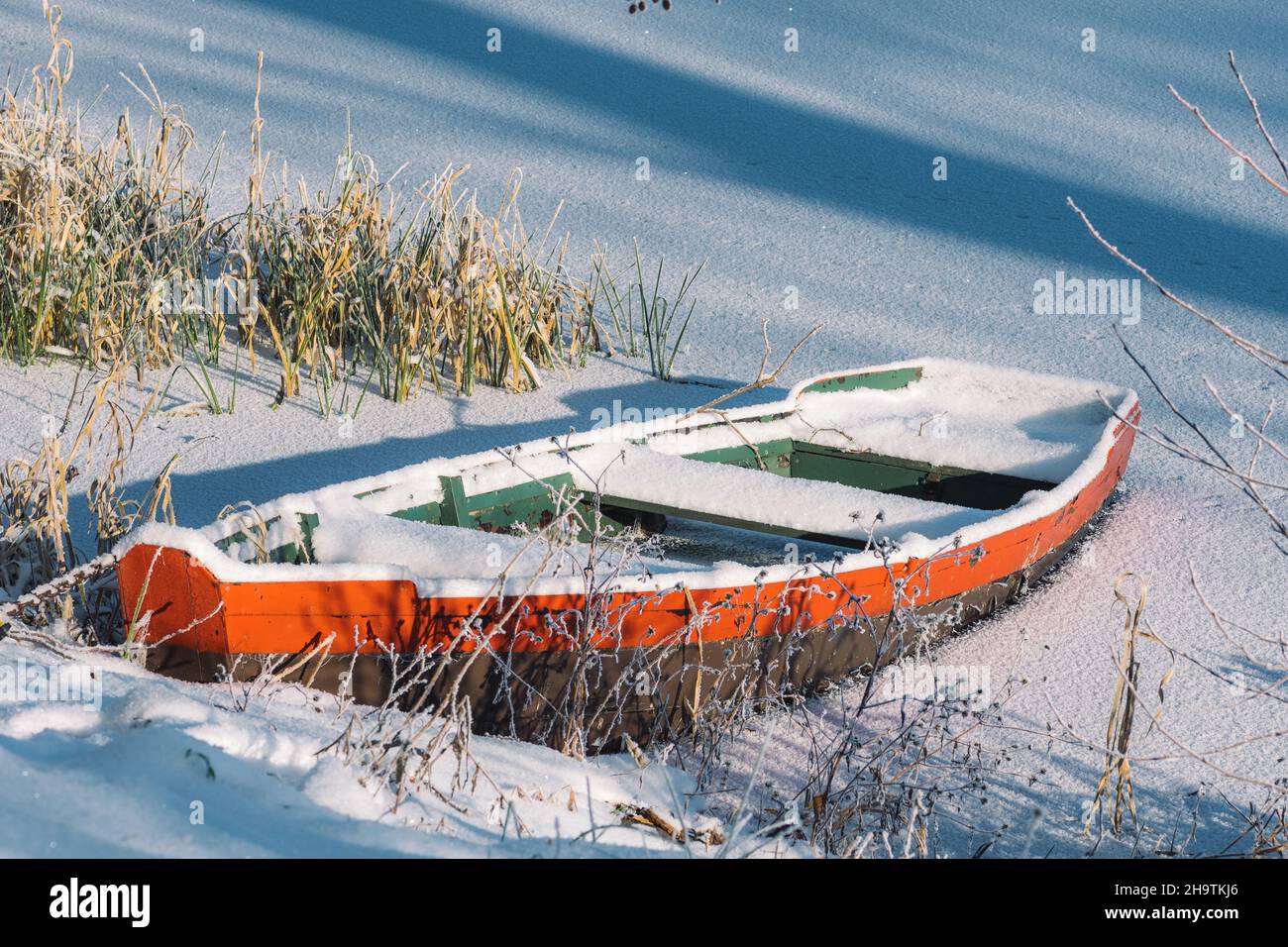 Wooden colorful boat stacked on a frozen lake covered by snow on the ...