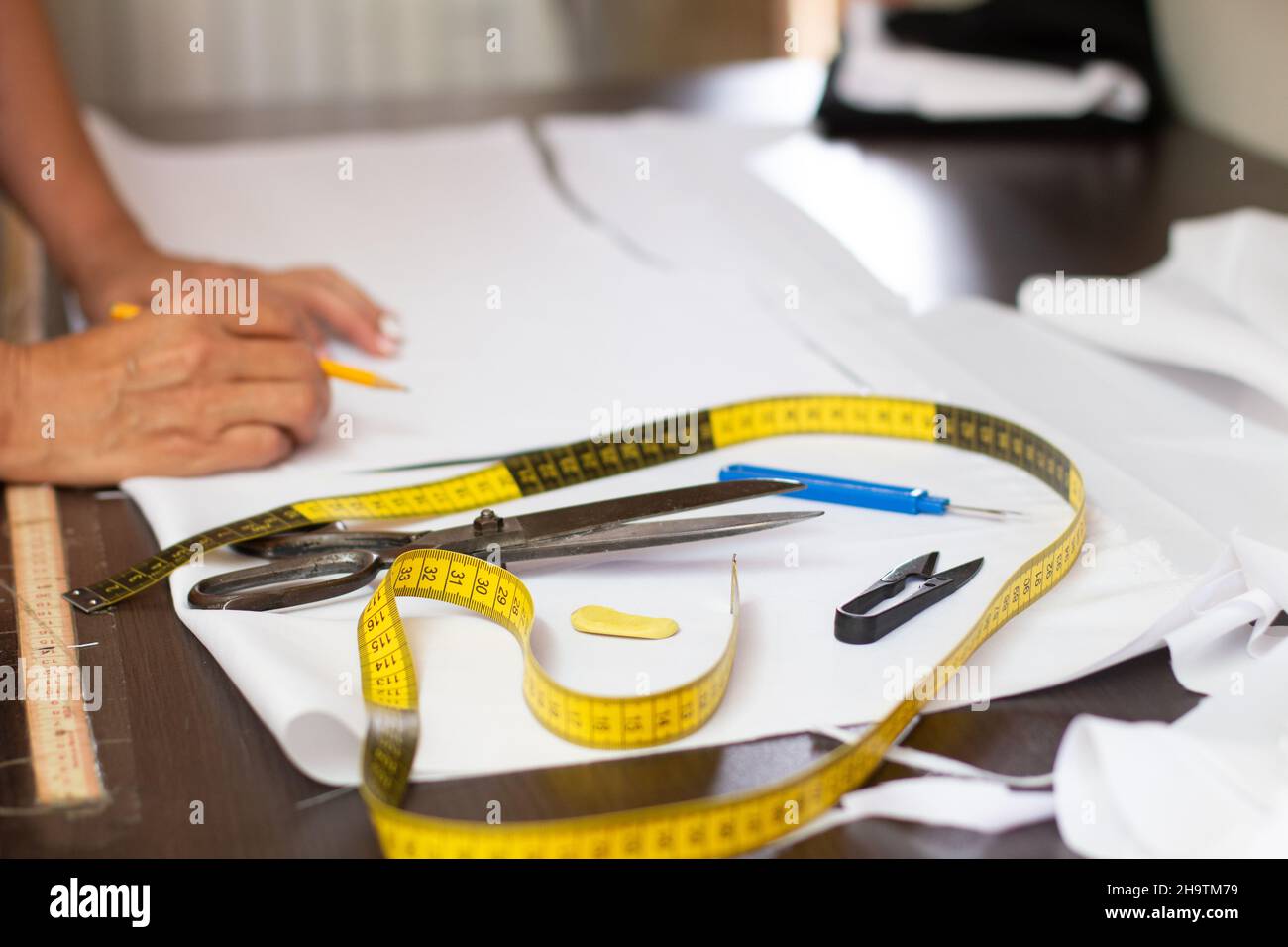 Dressmaking accessories on a fabric cutting table next to white fabric ...