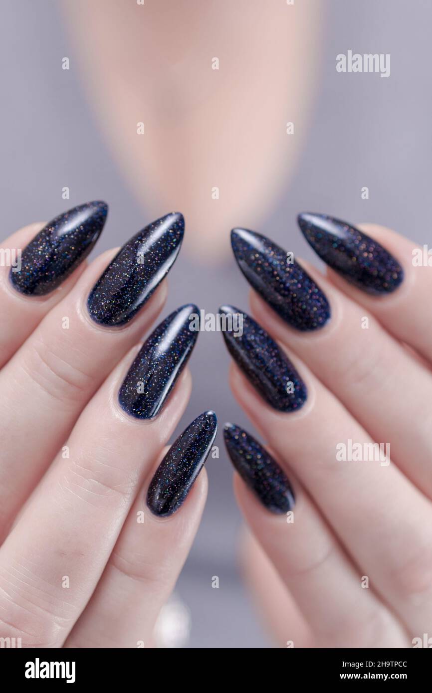 Female hand with long nails and dark blue black manicure holds a bottle ...