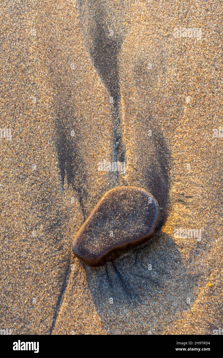 single pebble on sandy beach, solitary stone on sand at coast, patterns ...
