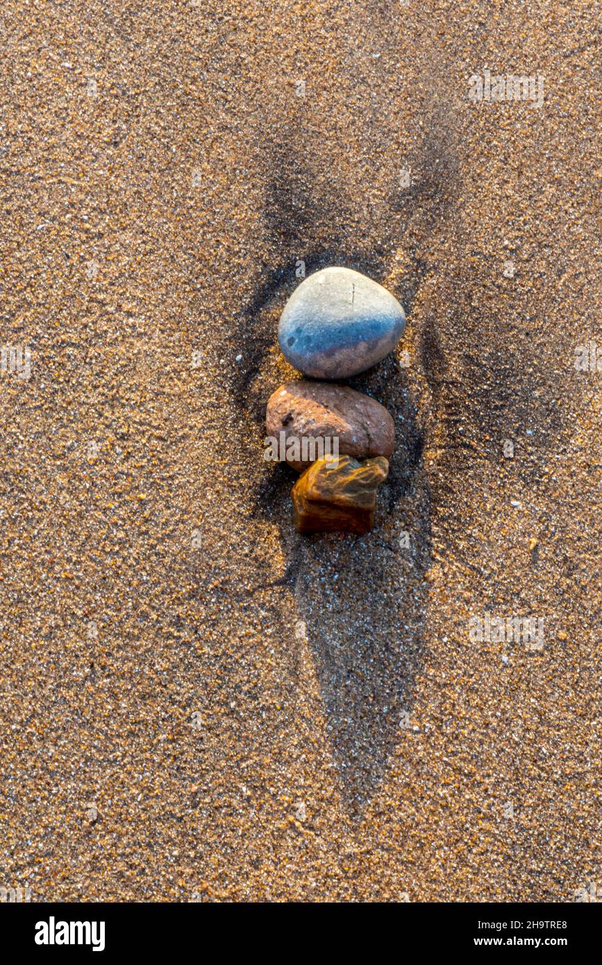 group of pebbles stranded on a sandy beach with patterns in the sand ...