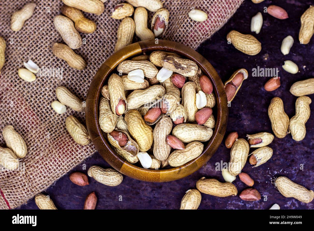 Top view of raw unpeeled peanut nuts in nutshell in brown round wooden ...
