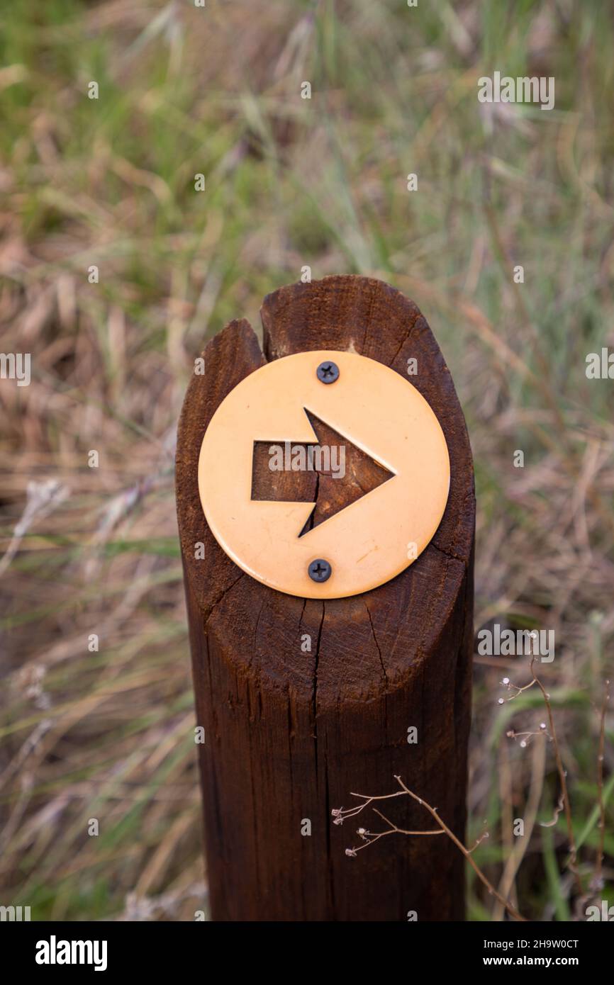 Faded orange plastic arrow mounted on a wooden pole. the arrow is ...