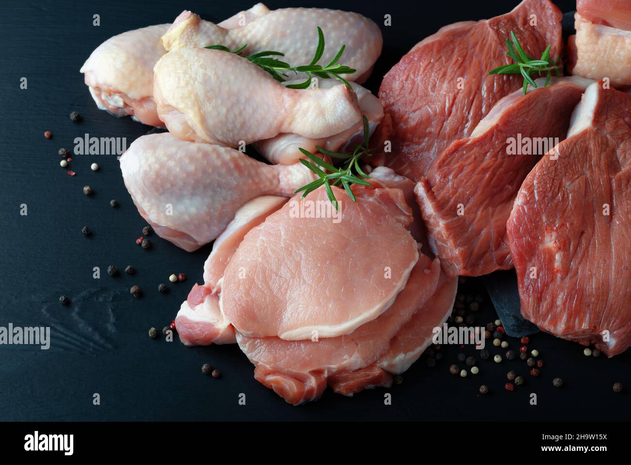 Various types of fresh meat: pork, beef, and chicken on a black table ...