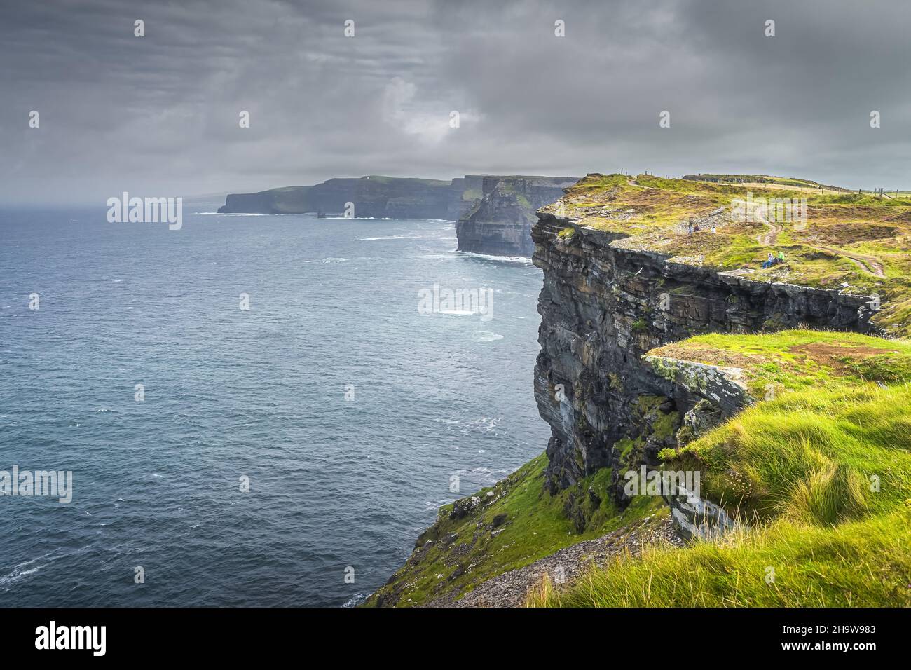 Small group of people on Cliffs of Moher with storm clouds overhead ...