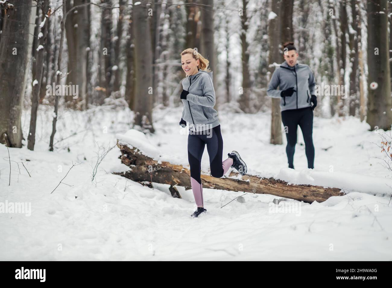 Sportswoman racing her friend in forest at snowy winter day. Fitness ...