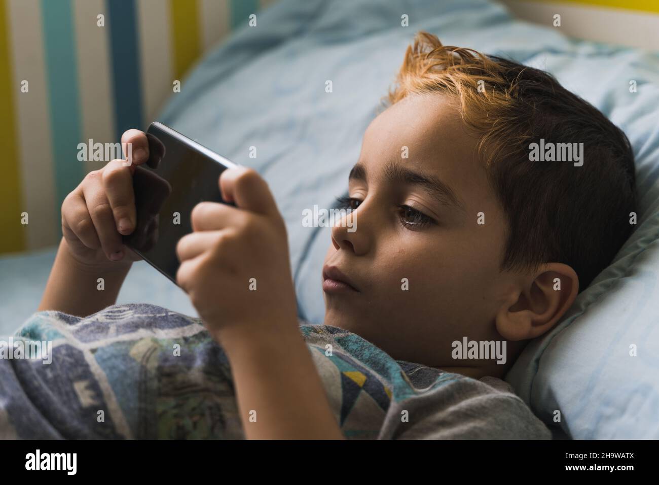 Little kid playing game on smartphone chilling on bed Stock Photo - Alamy