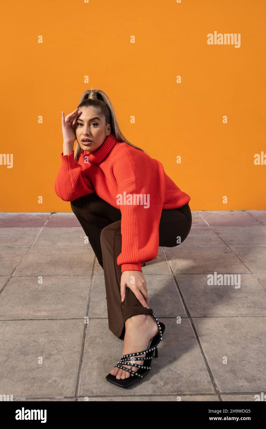 Vertical shot of an attractive Spanish model in a squatting pose in the ...