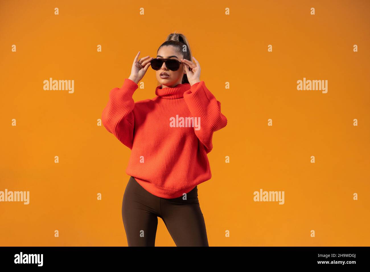 Fancy Spanish lady wearing an orange sweater and sunglasses is posing ...