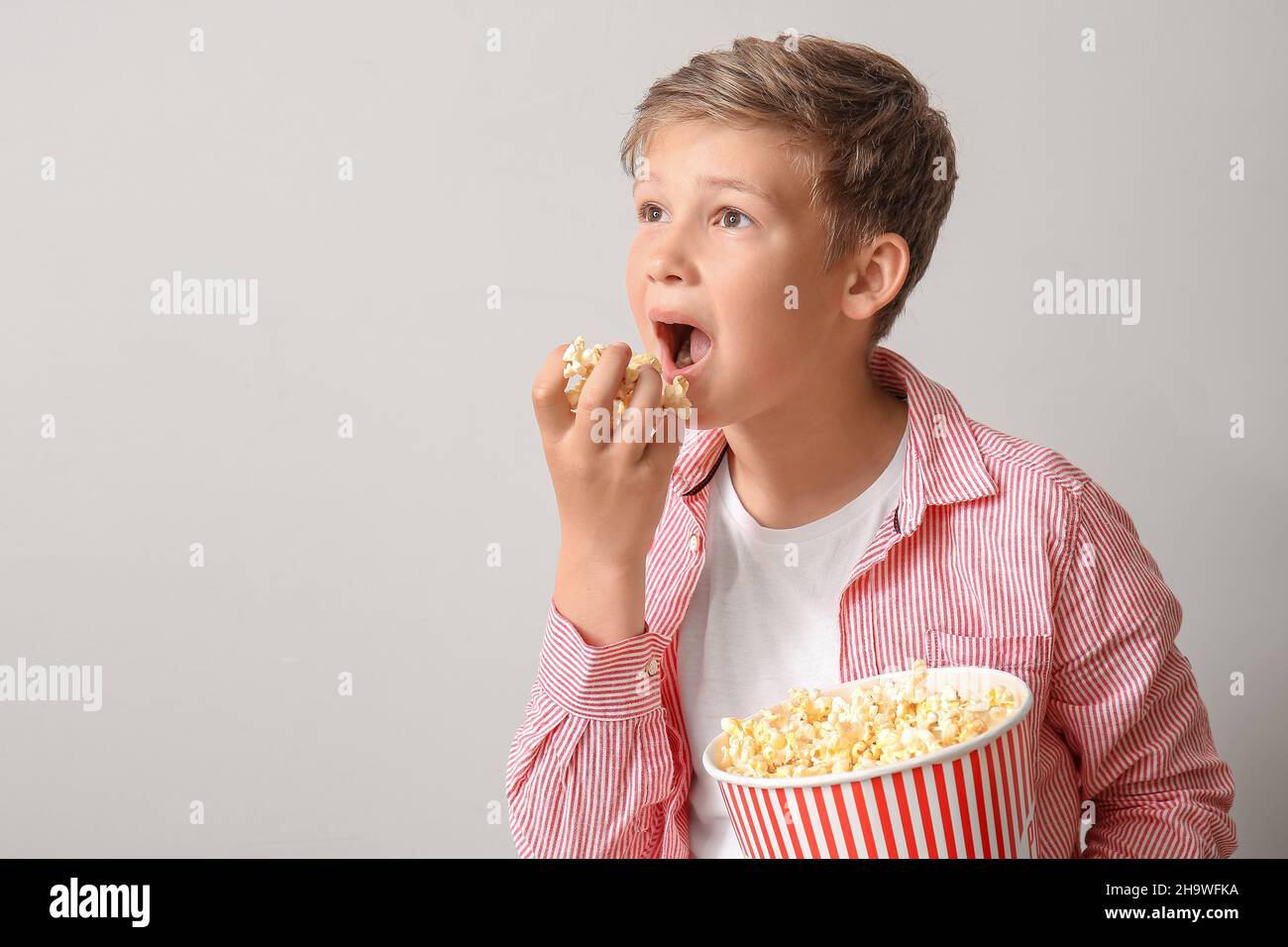 Little boy eating tasty popcorn on light background Stock Photo - Alamy