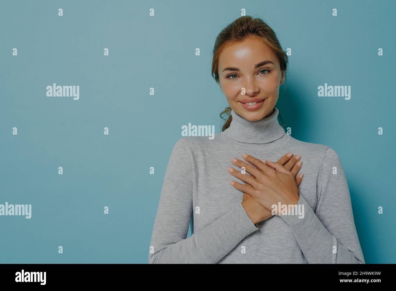 Attractive young smiling woman holding folded hands near heart on chest ...