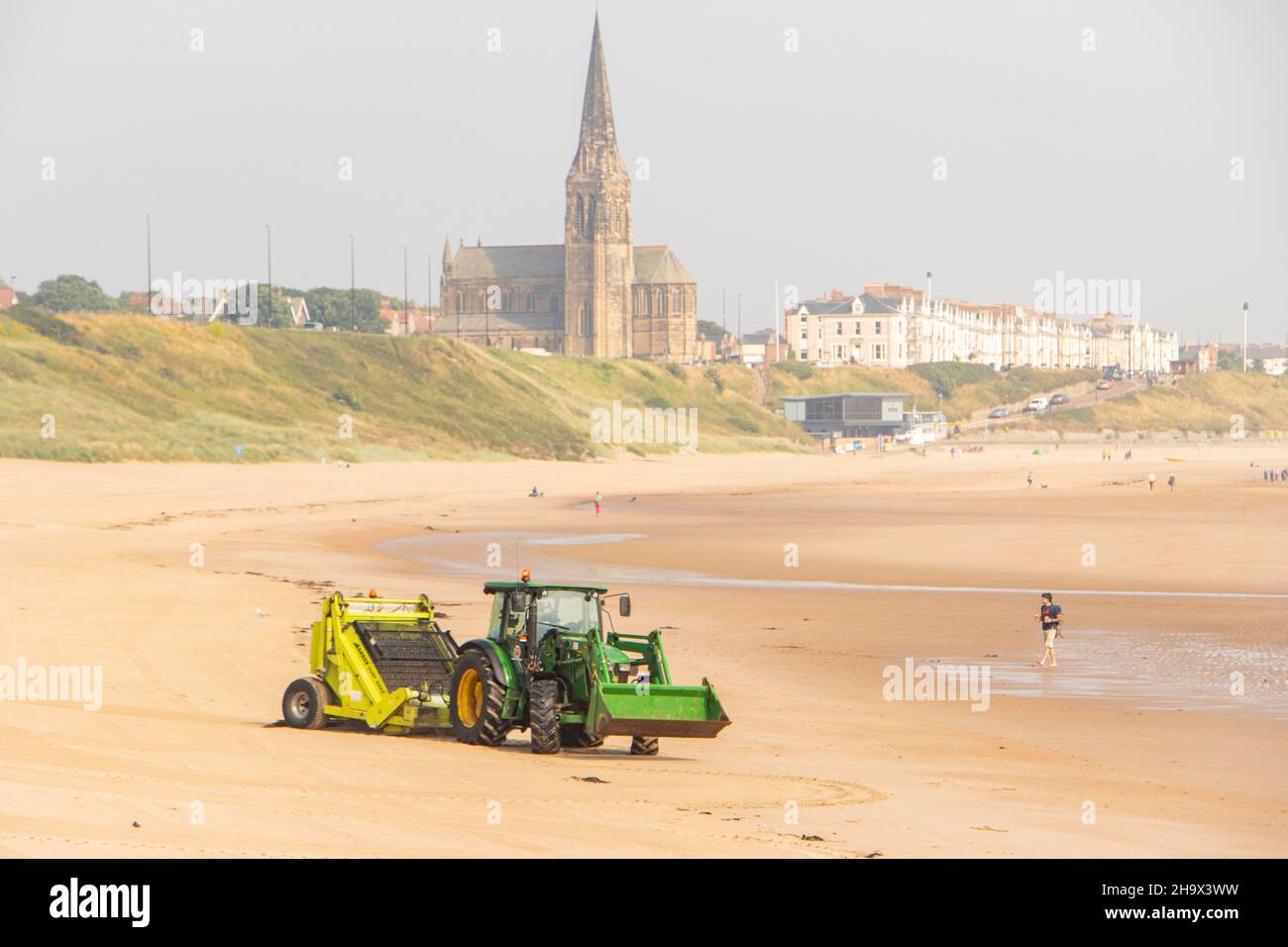 tractor grading or raking the sand on the beach in Tyneside with church ...