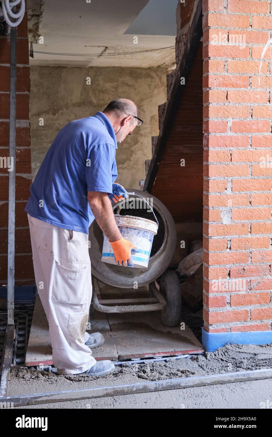 Construction worker with a bucket in his hands loads a concrete mixer ...