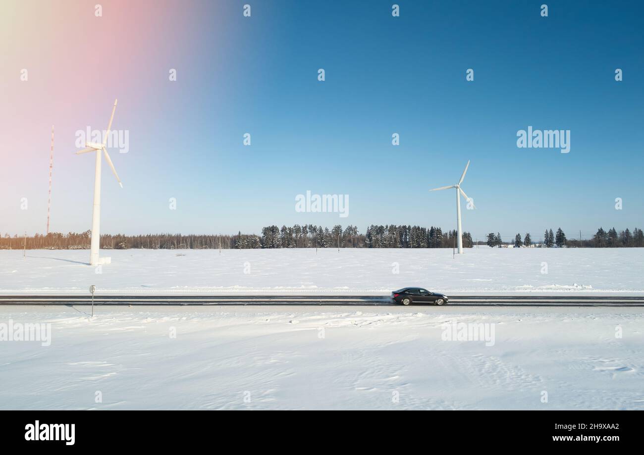 Car moving on snowy road with blue sky and electric wind plant ...