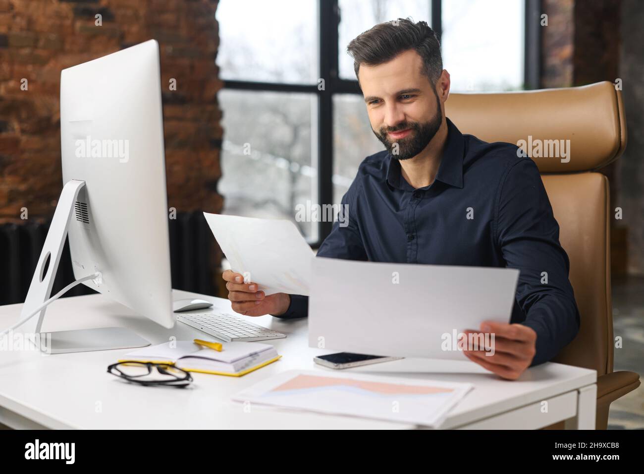 Smiling male office employee doing paperwork sitting at the desk ...