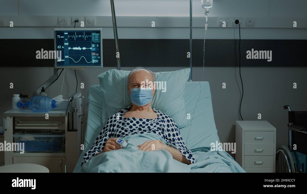 Portrait of old patient with face mask sitting in hospital ward ...