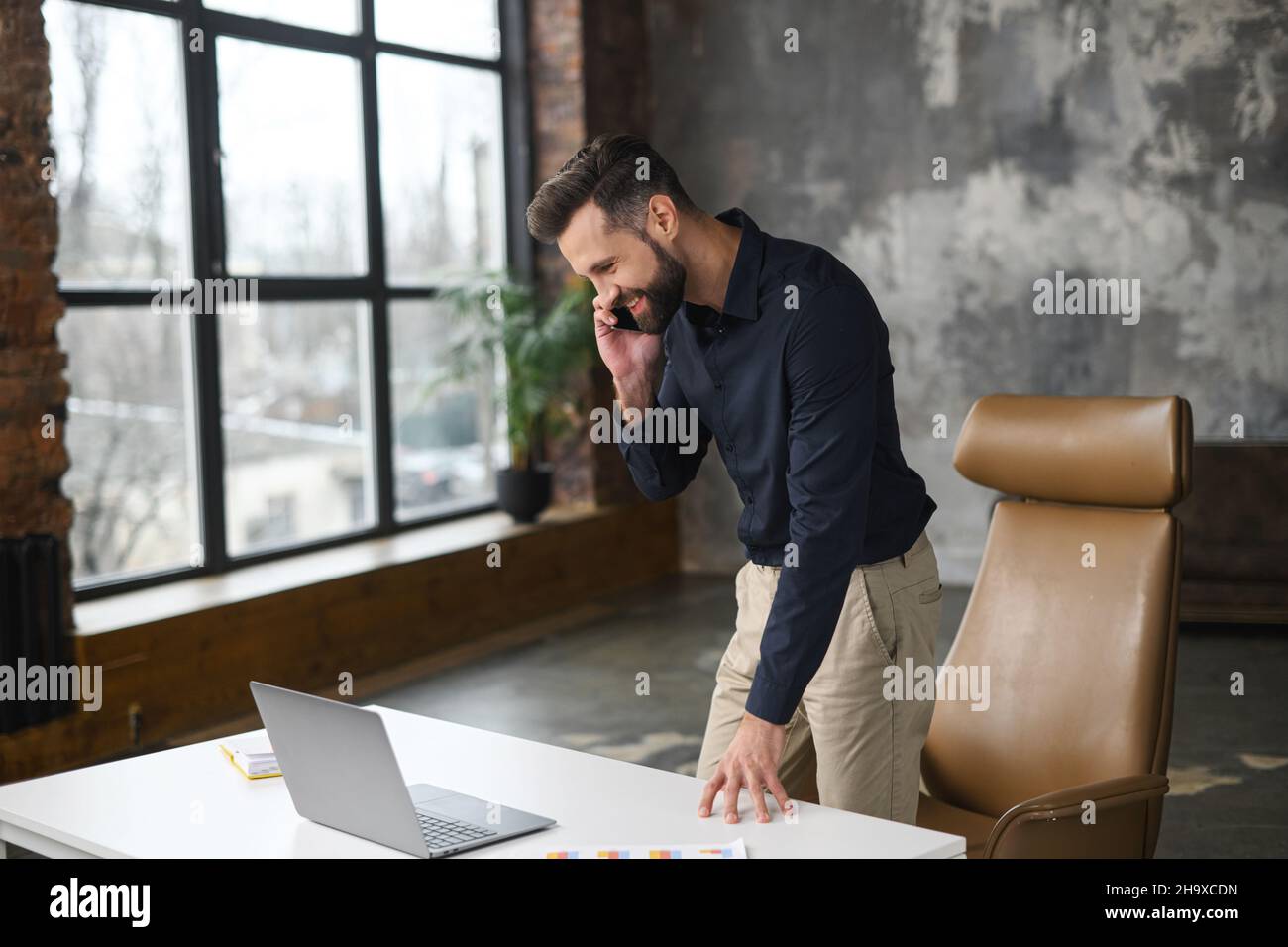 Busy male office employee standing near office desk, talking on the ...