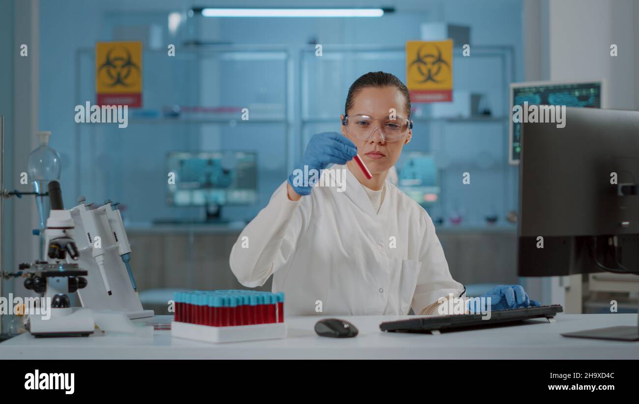 Woman scientist analyzing liquid in test tube and using computer for ...