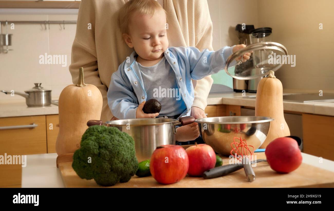 Cute smiling baby boy with mother playing with pans and utensils on ...