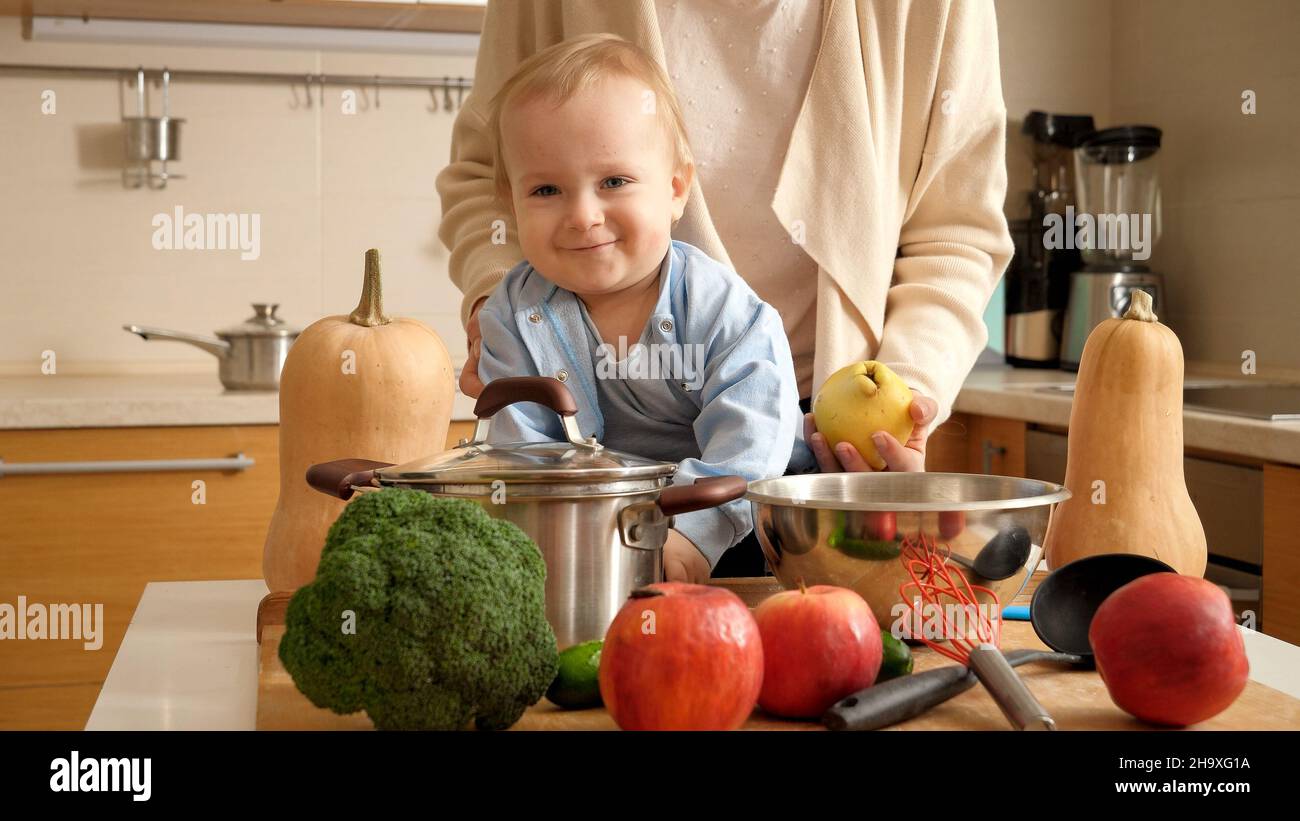Adorable smiling baby boy sitting on kitchen table full of vegetables ...