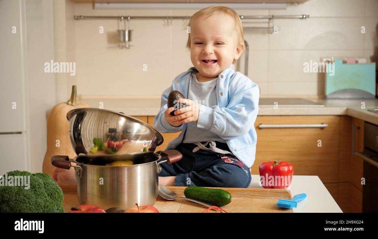 Cute smiling baby boy sitting on wooden kitchen table and playing with ...
