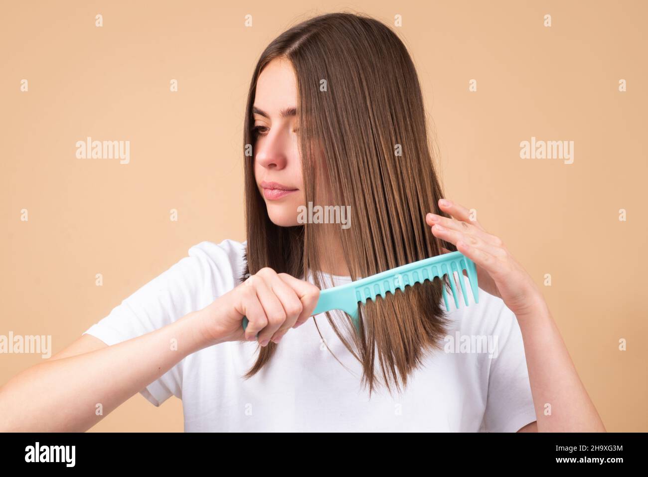 Young woman combing healthy and natural shiny hair, isolated on studio ...