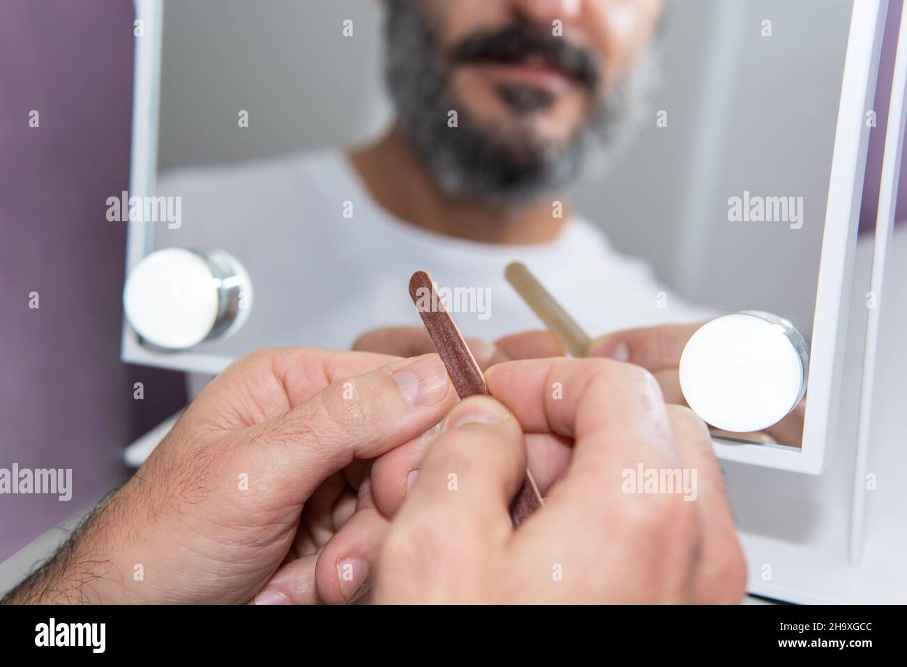 Mature Caucasian bearded man filing his hand nails in front of a mirror ...
