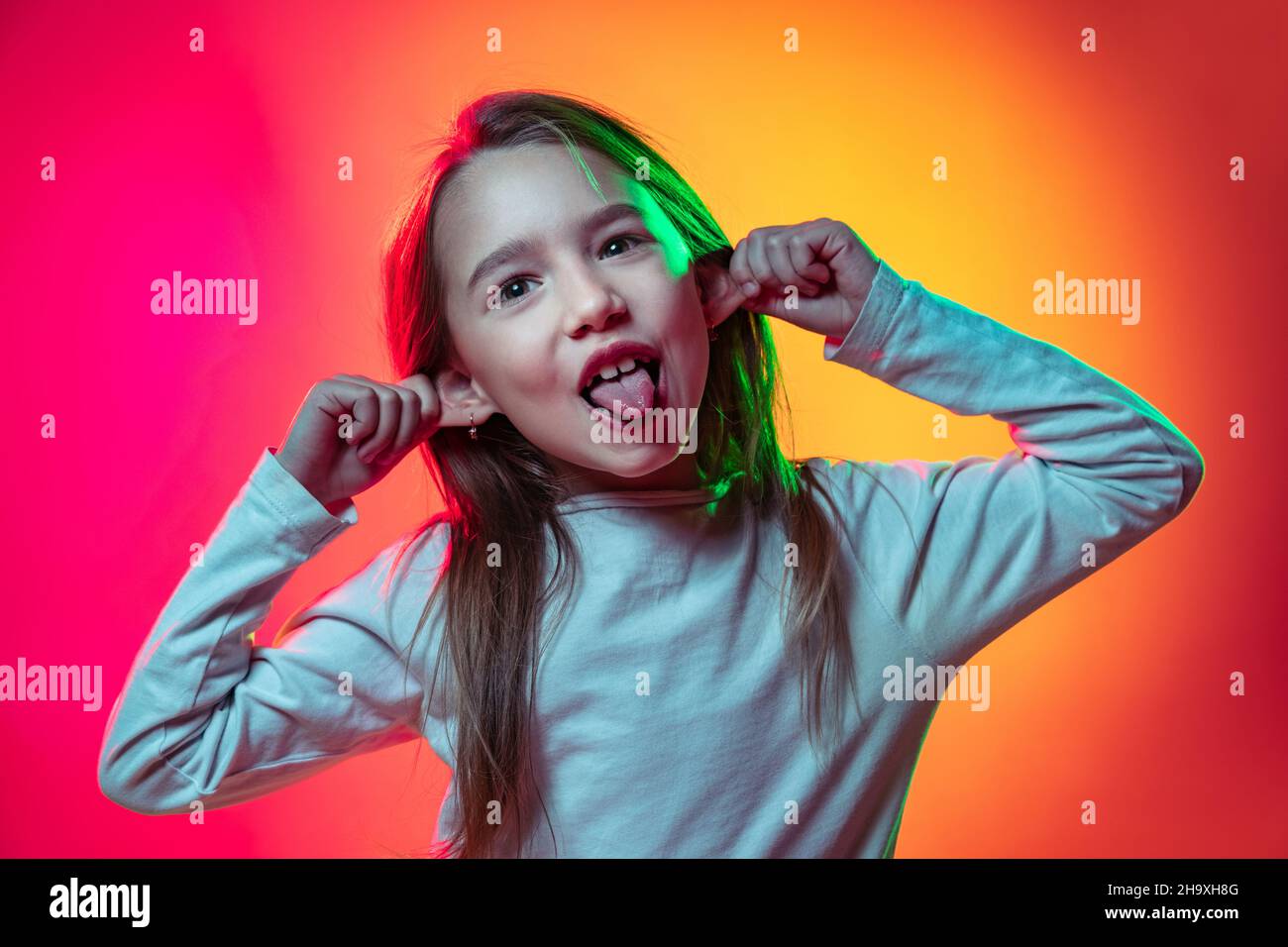 One funny preschool girl, happy kid making faces isolated on red yellow ...