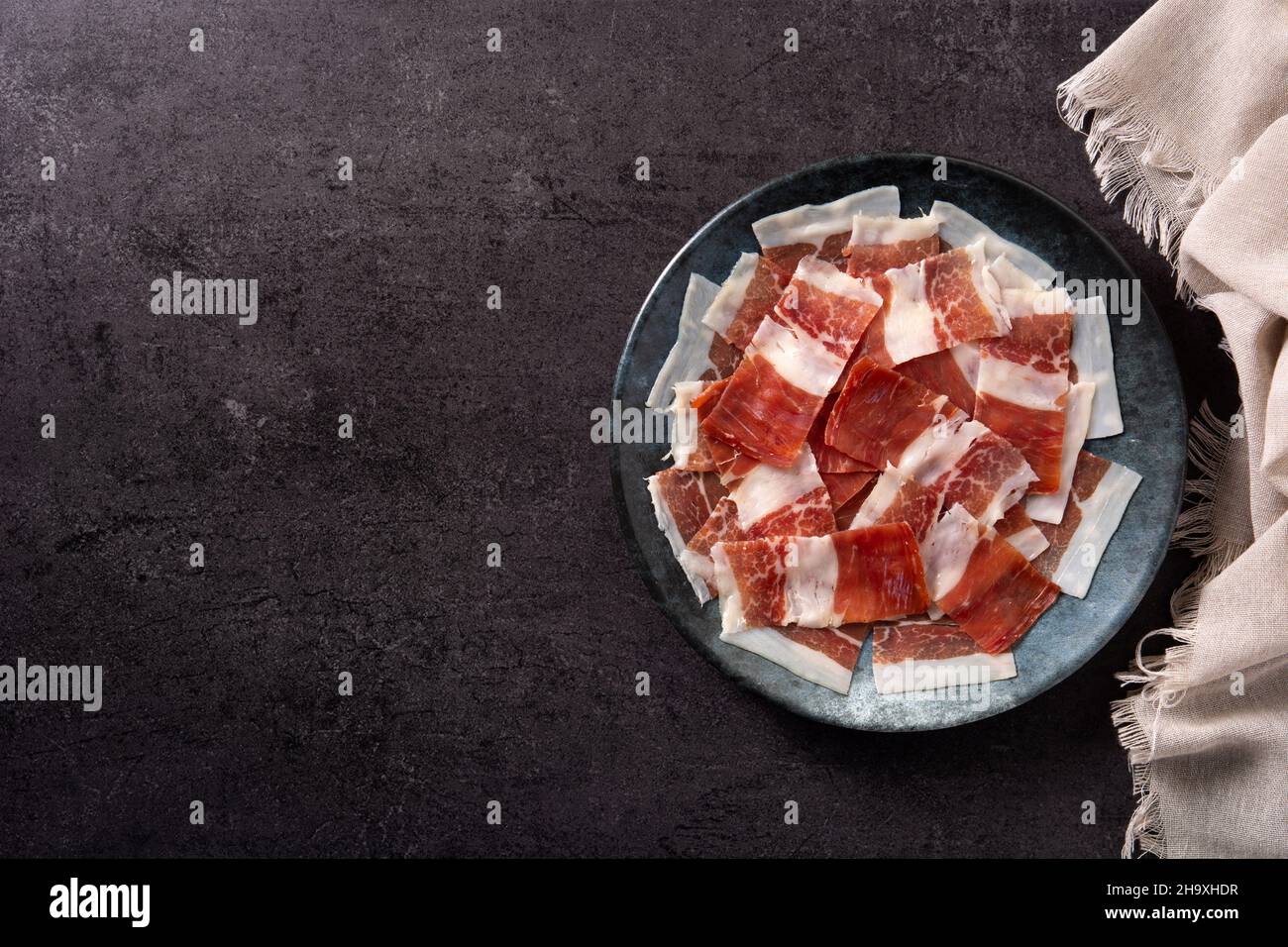 Spanish serrano ham slices on black plate on black slate background ...
