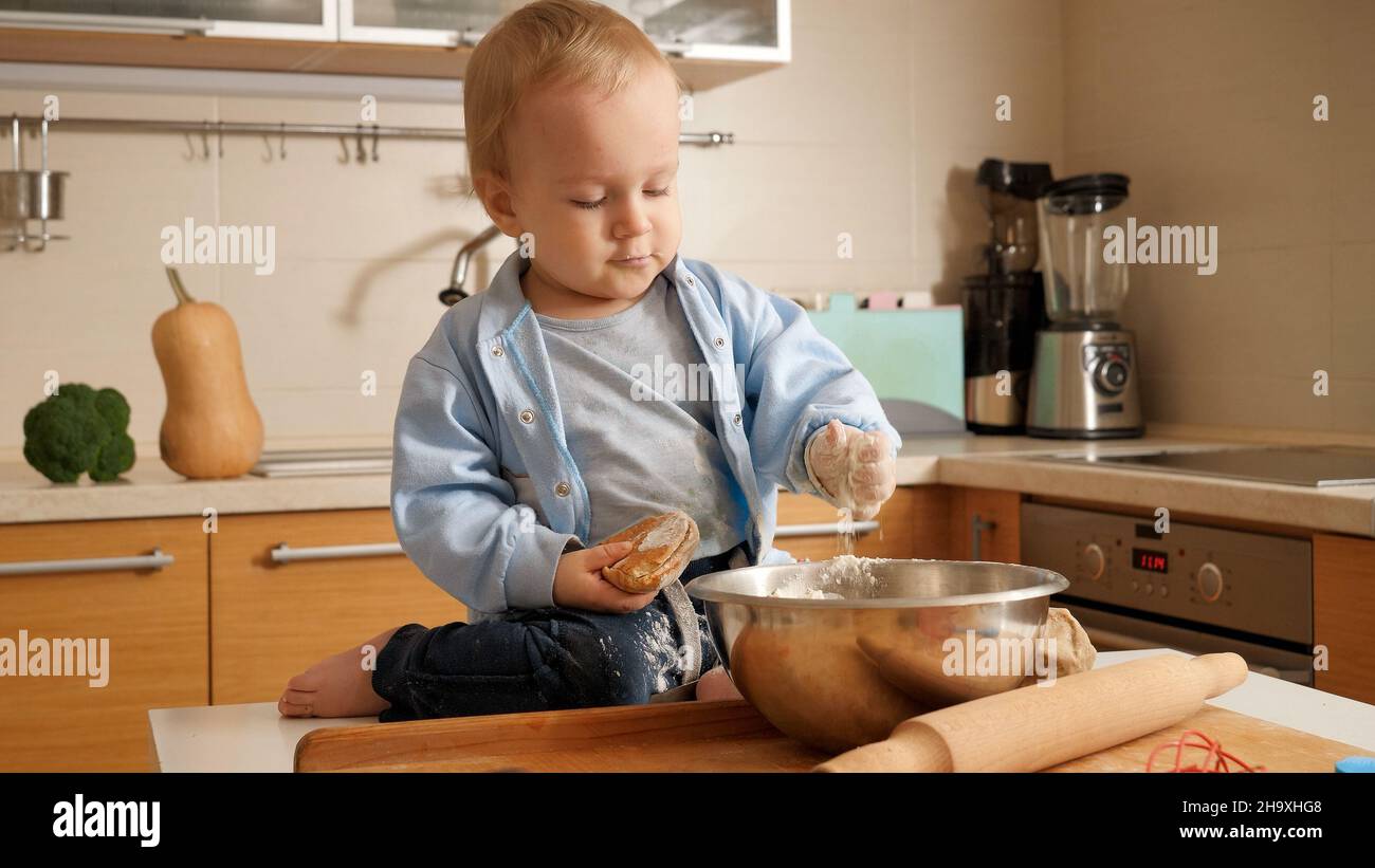 Funny little baby boy playing with flour in bowl while cooking bread on ...