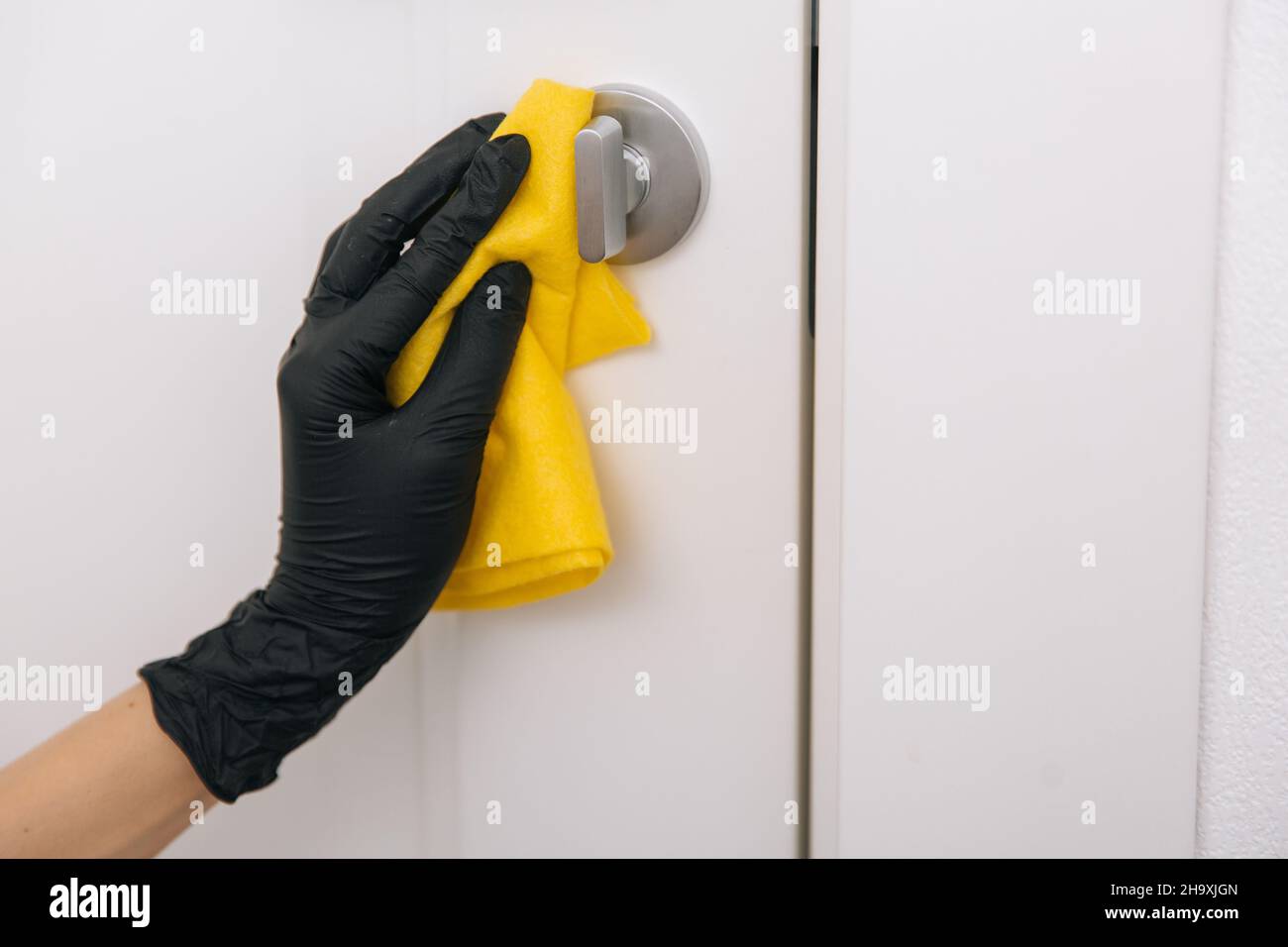 Cleaning door handle with yellow wipe in black gloves. Woman hand using ...
