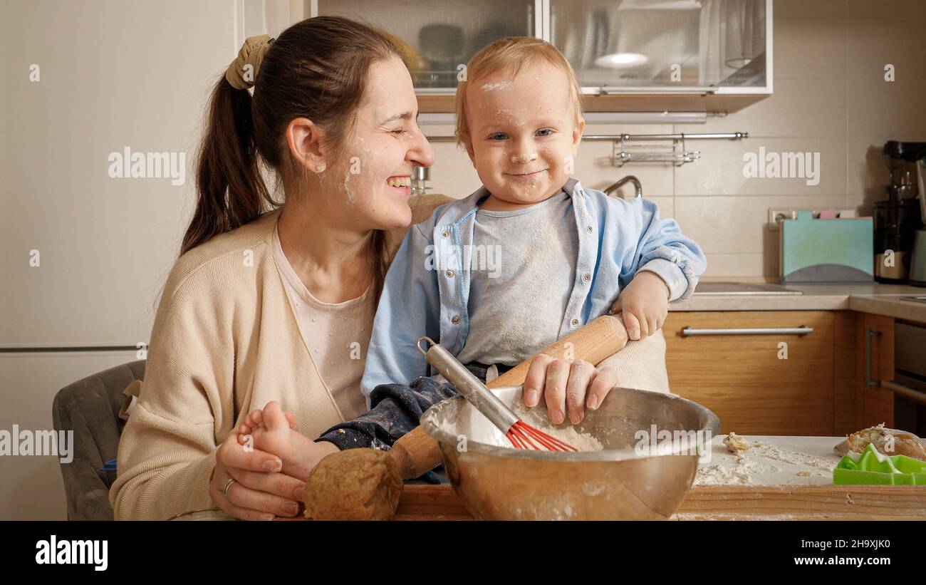 Happy smiling baby boy with mother kneading dough for baking bread on ...