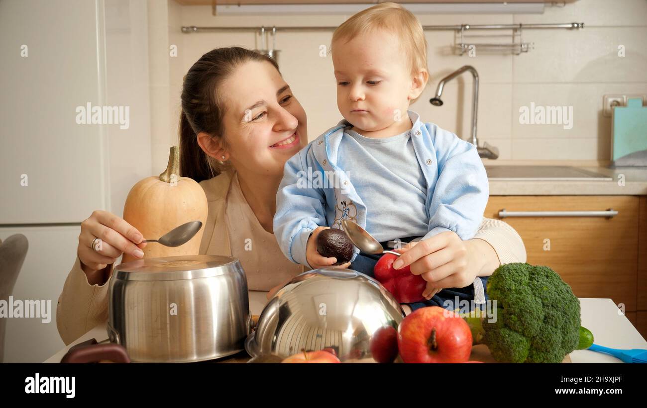 Happy smiling mother with baby son playing with spoons on pans in ...