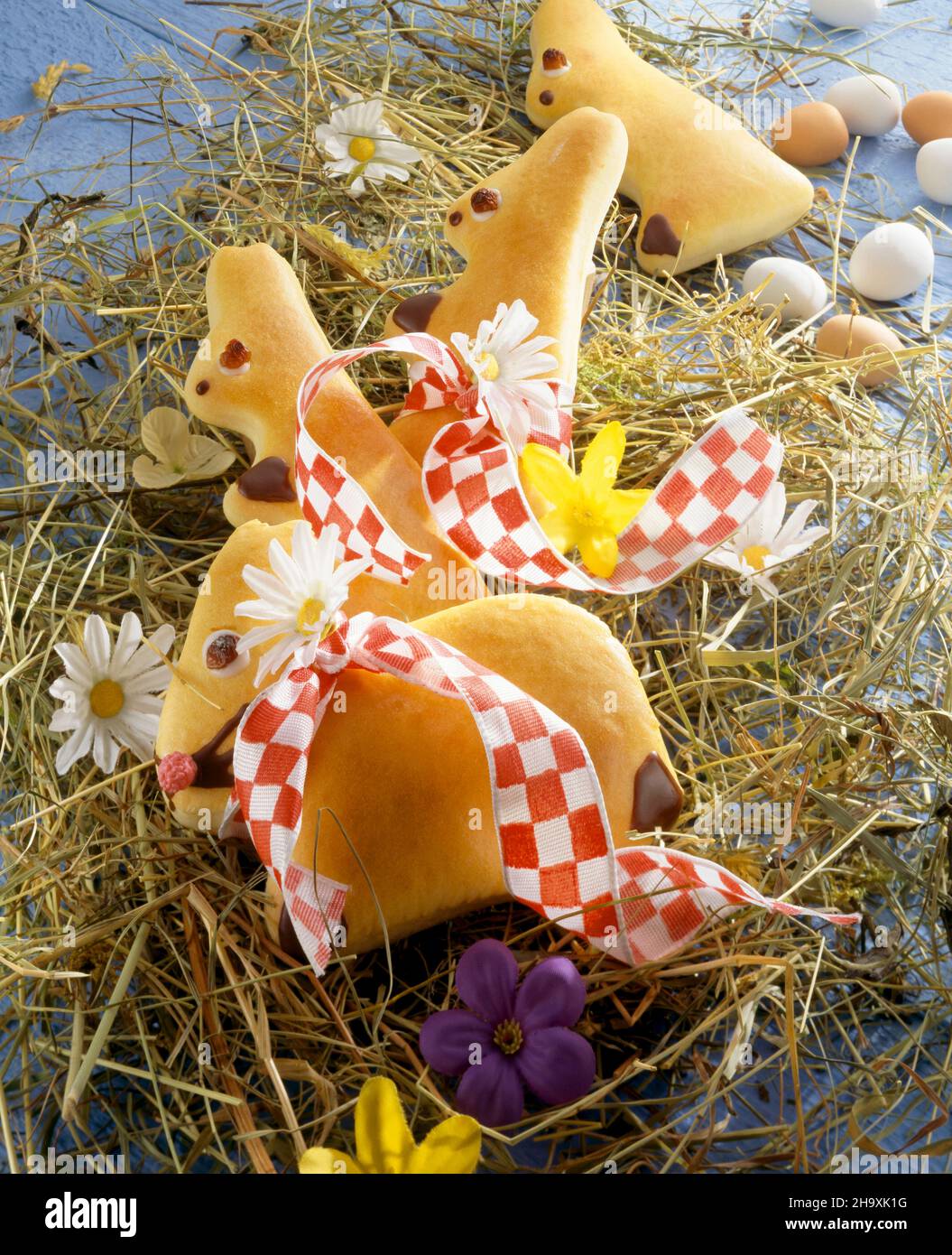 Sweet yeast dough Easter bunnies on hay with spring flowers Stock Photo ...