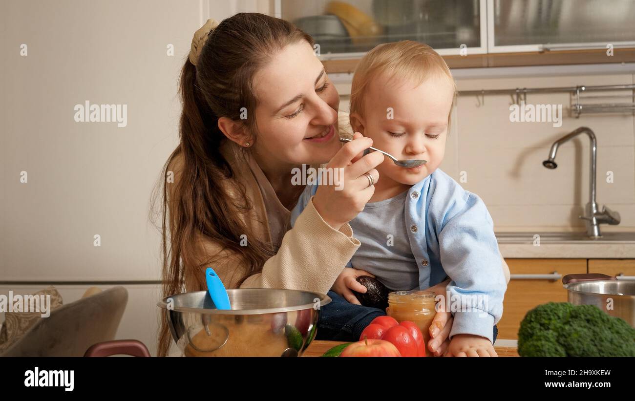 Cute baby boy sitting on kitchen table and playing with cookware while ...