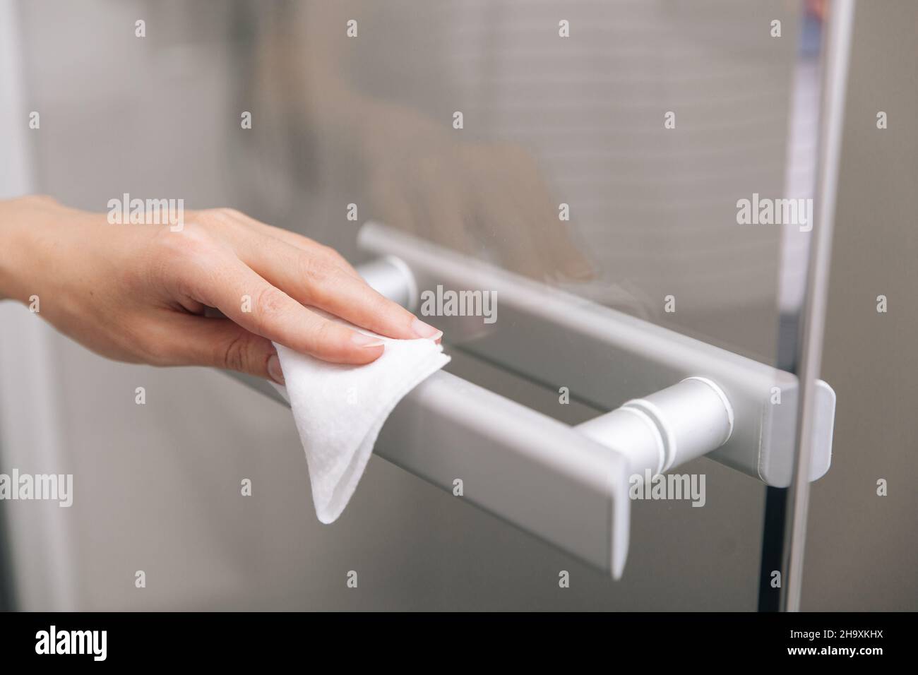 Cleaning glass door handles with an antiseptic wet wipe. Woman hand ...