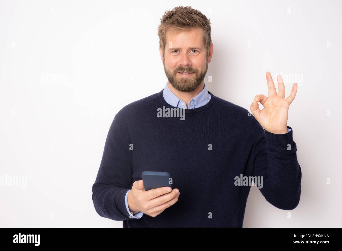 Young smiling handsome man using smartphone with okay sign standing ...