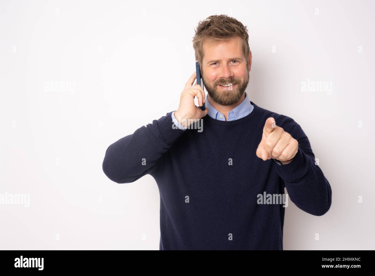 Young smiling handsome man talking on mobile phone pointing finger to ...