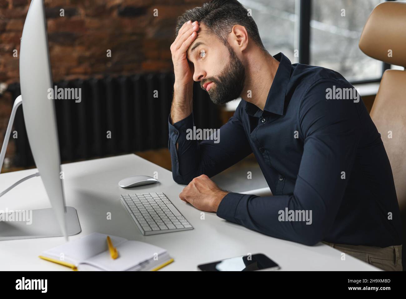 Depressed young male office employee is staring at computer monitor ...