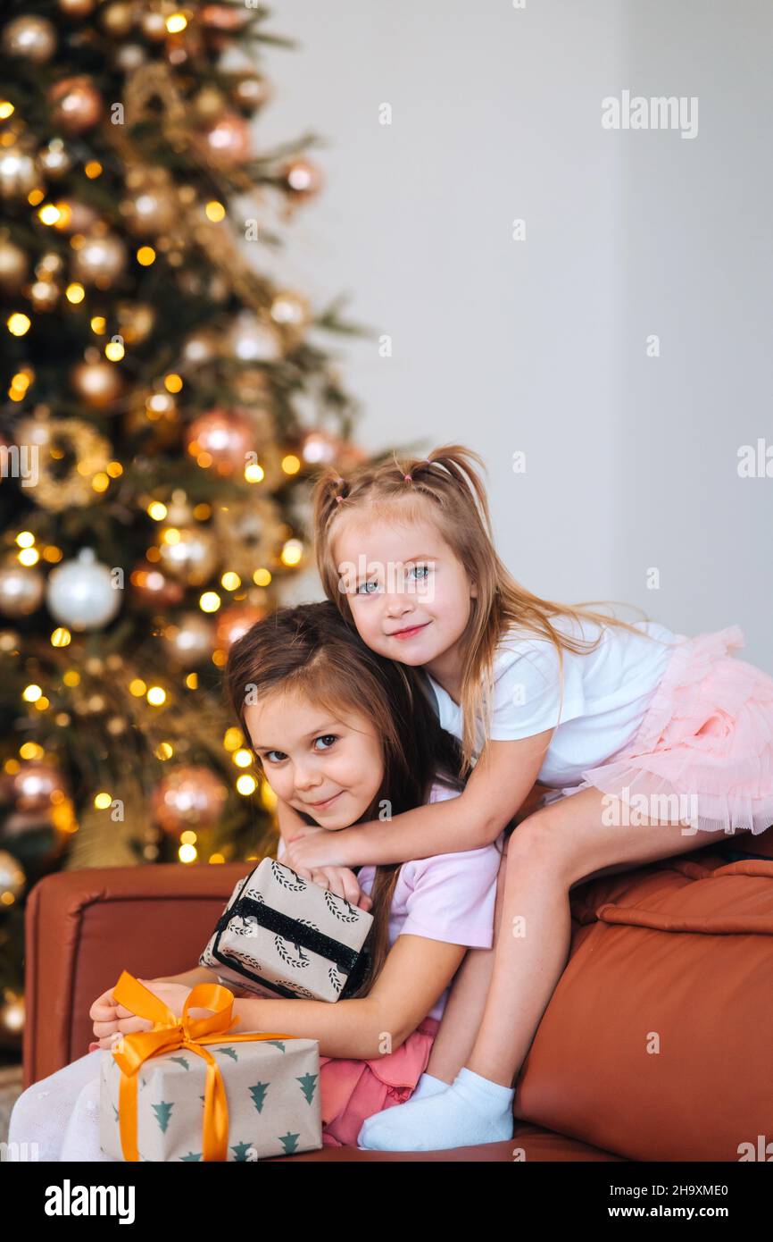 Two little girls are playing with New Year's gifts by the tree at sofa ...