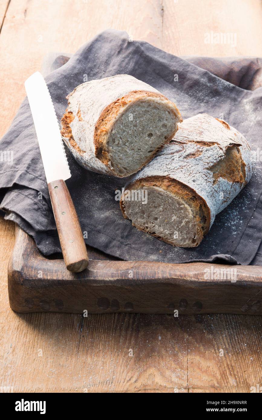 Two rustic loaves of bread on a linen cloth on a wooden tray with a ...