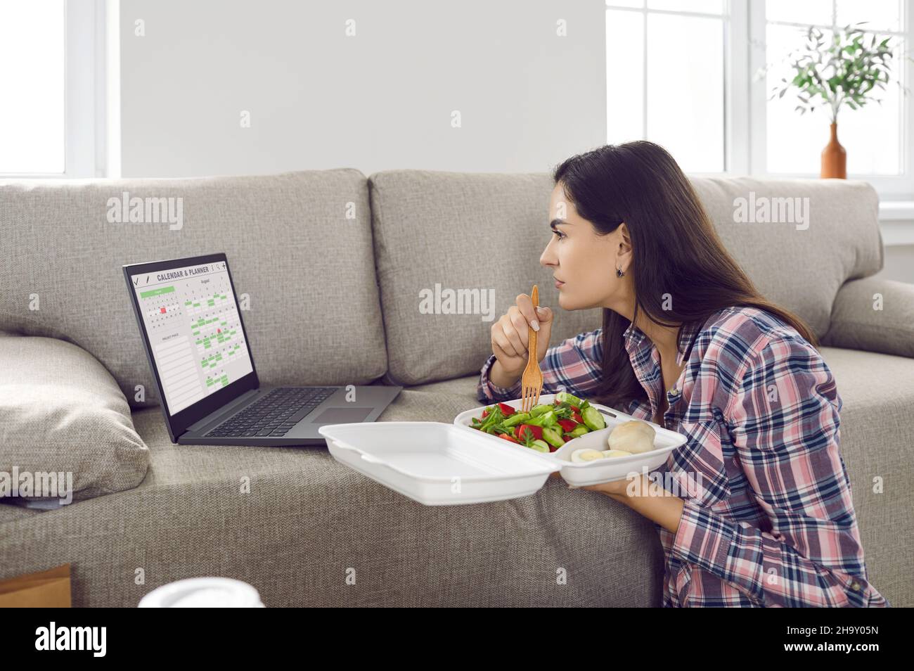 Busy woman using calendar and planner on laptop while eating takeaway ...