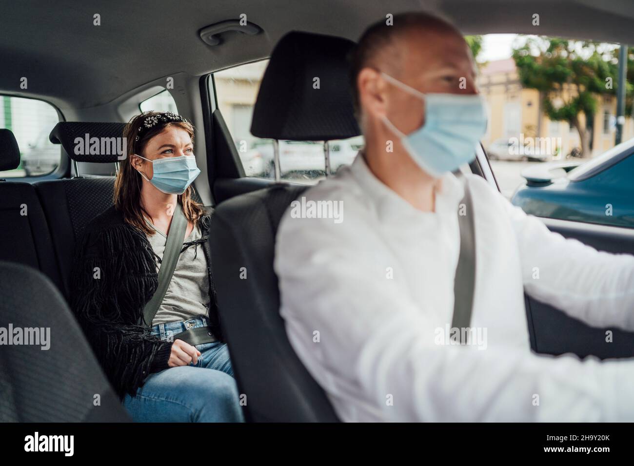 Taxi driver in a mask with a female client on the back seat wearing ...