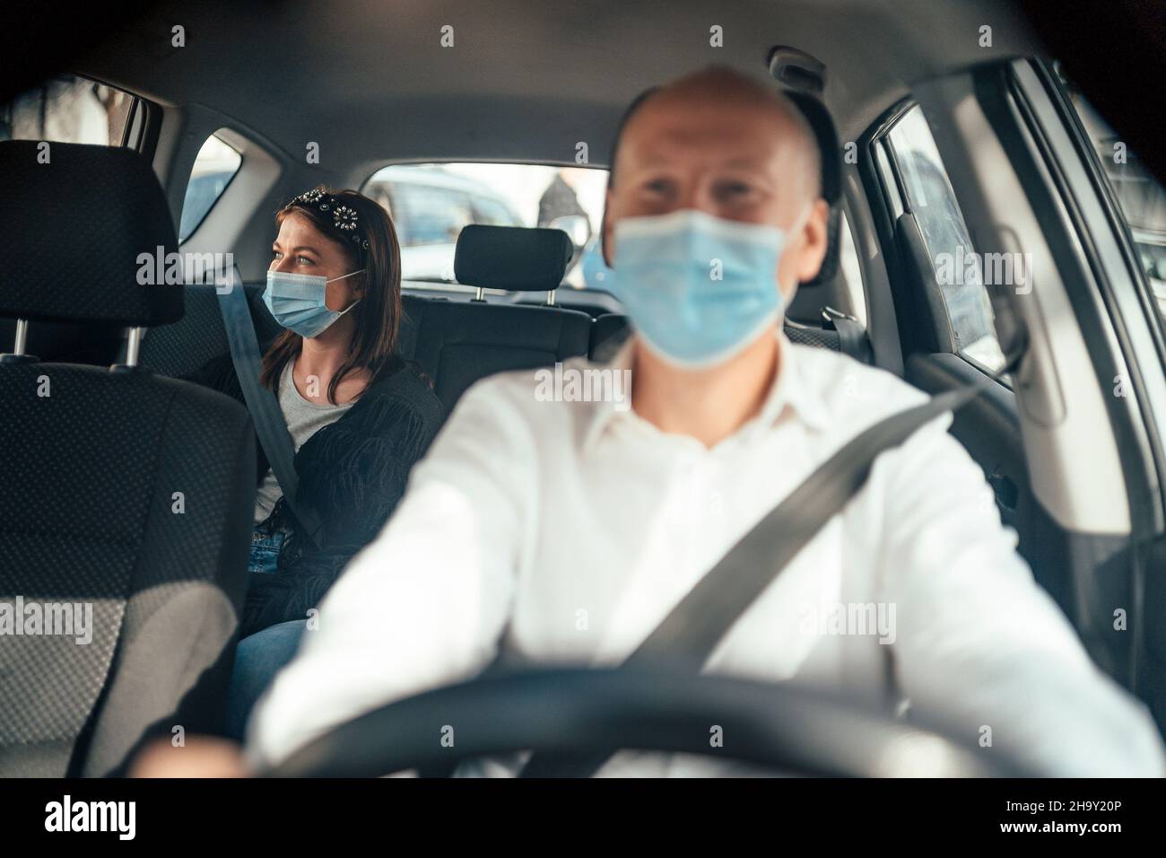 Taxi driver in a mask with a female client on the back seat wearing ...