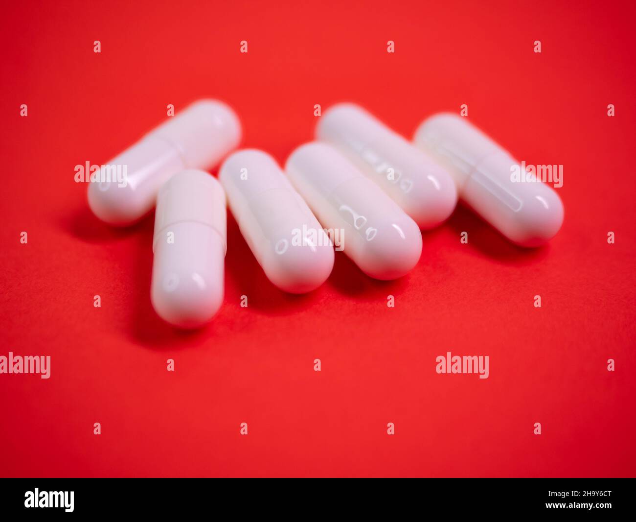 White drug capsules on colored red paper texture background. Macro ...
