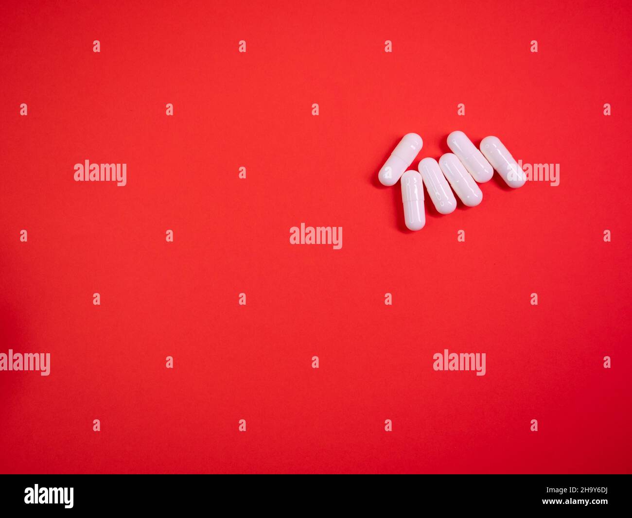 White drug capsules on colored red paper texture background. Macro ...