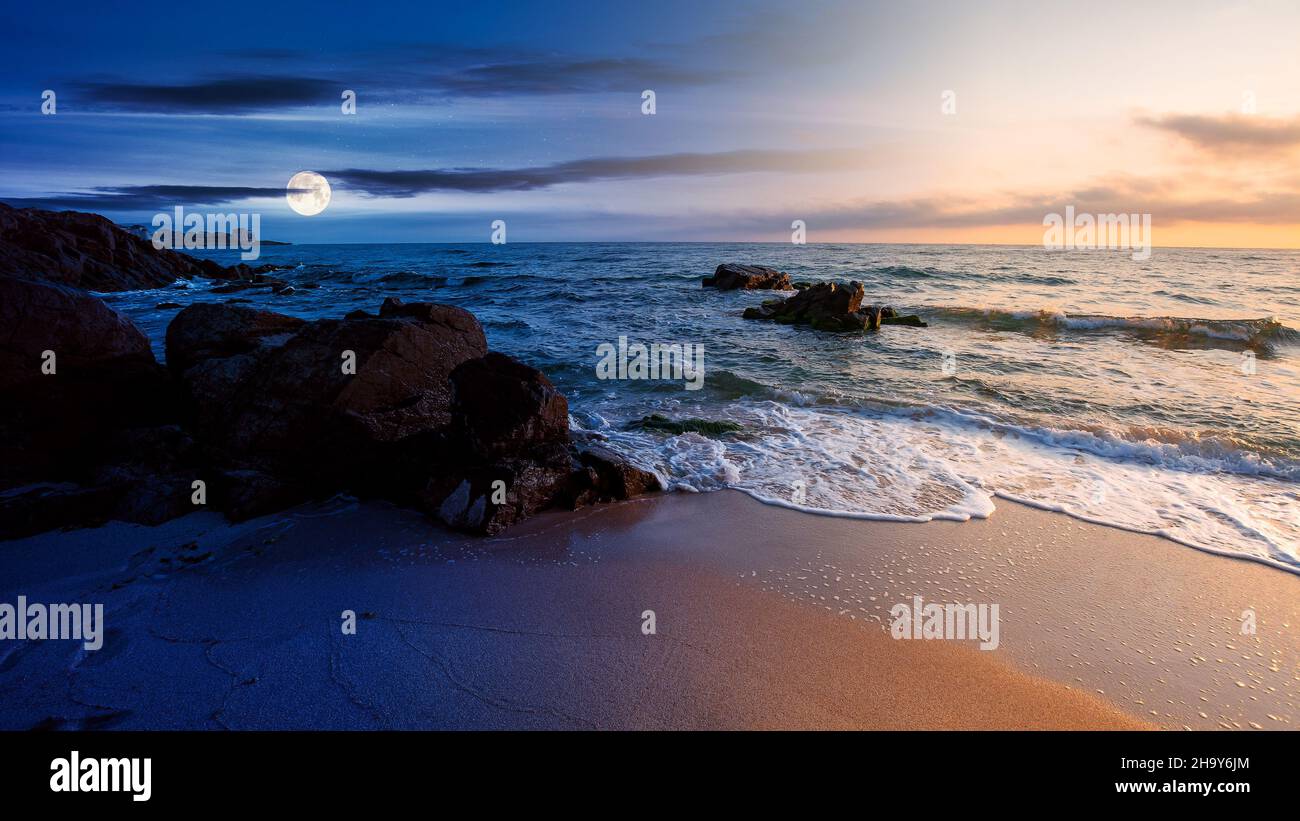 day and night time change concept above huge stones on the sandy beach ...