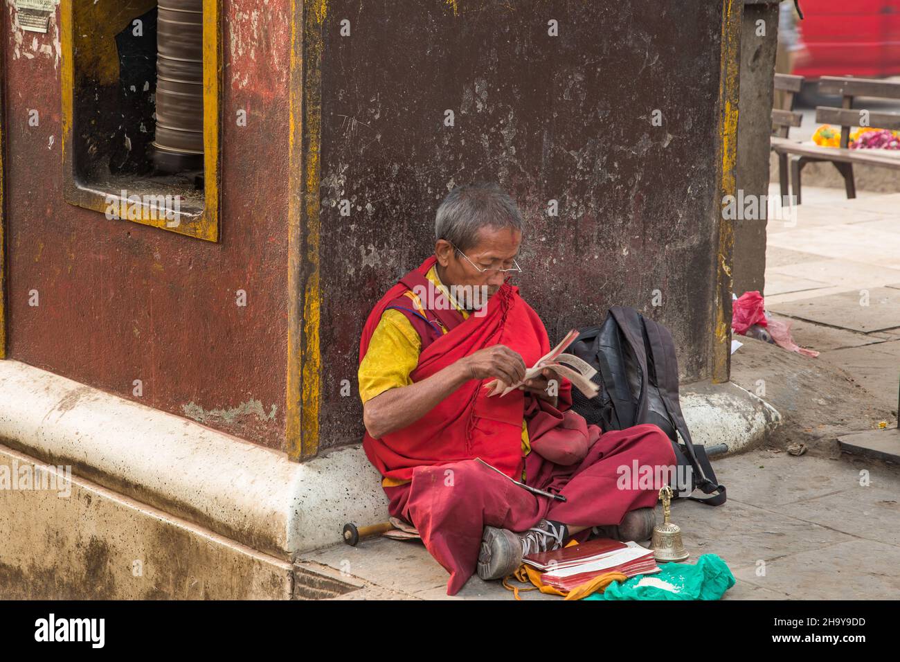 A Buddhist monk studies his scriptures by a prayer wheel in the ...