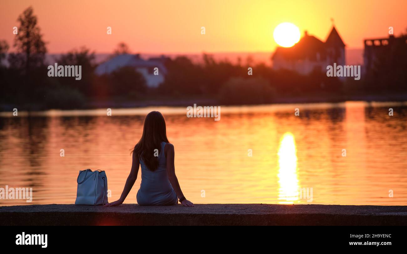 Lonely woman sitting alone on lake shore on warm evening. Solitude and ...