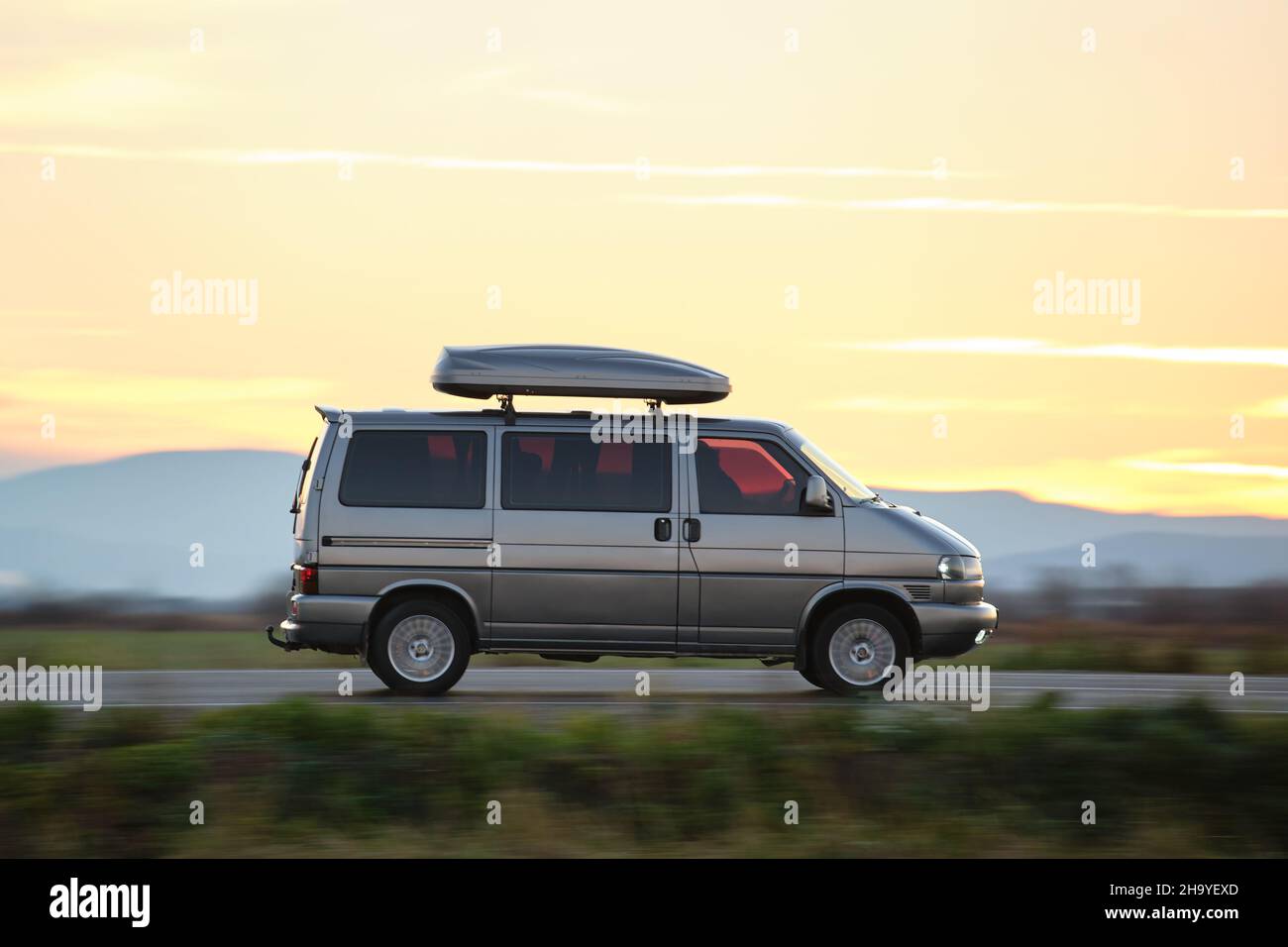 Passenger van with roof rack driving fast on intercity road at sunset ...